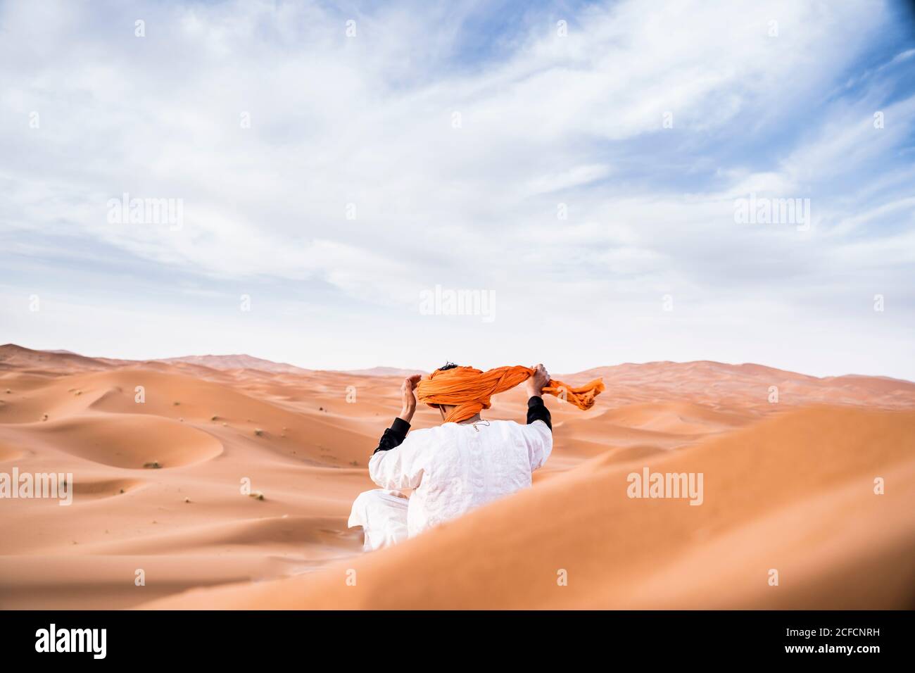Back view of man wearing long outfit adjusting a colorful turban ...