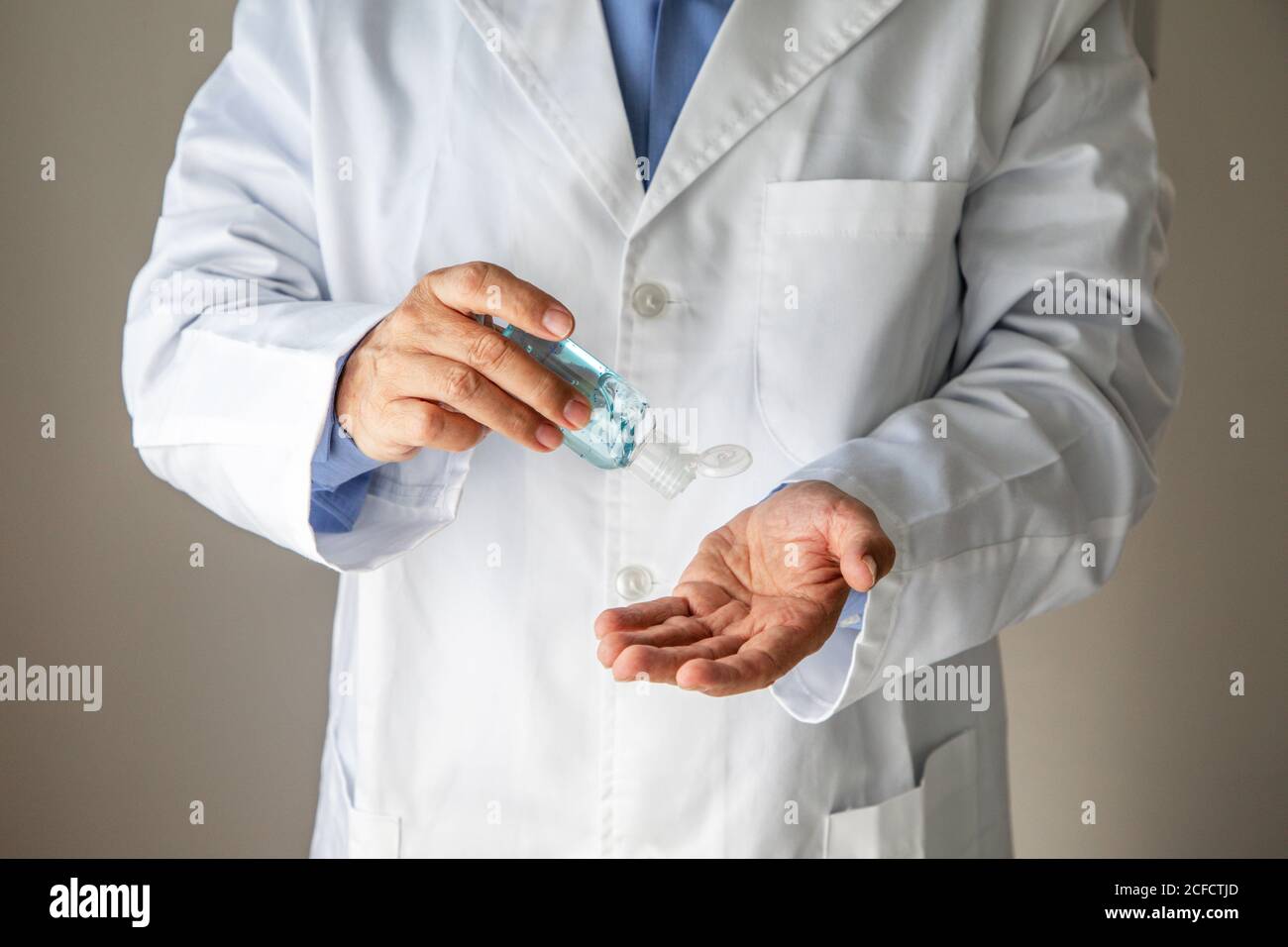 Crop male general practitioner in medical gown applying antibacterial ...