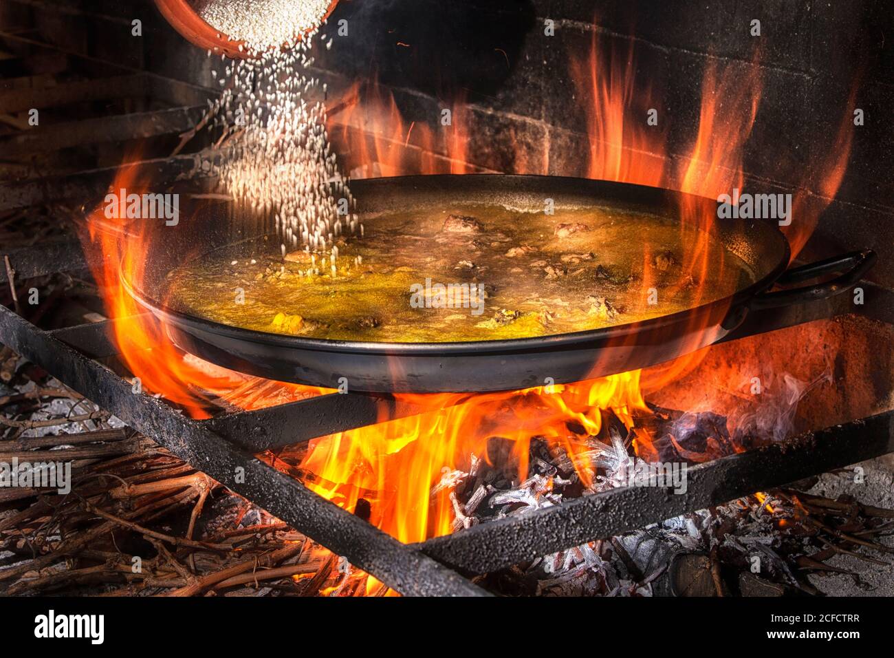 Adding rice into big iron pan with boiling broth for cooking paella ...