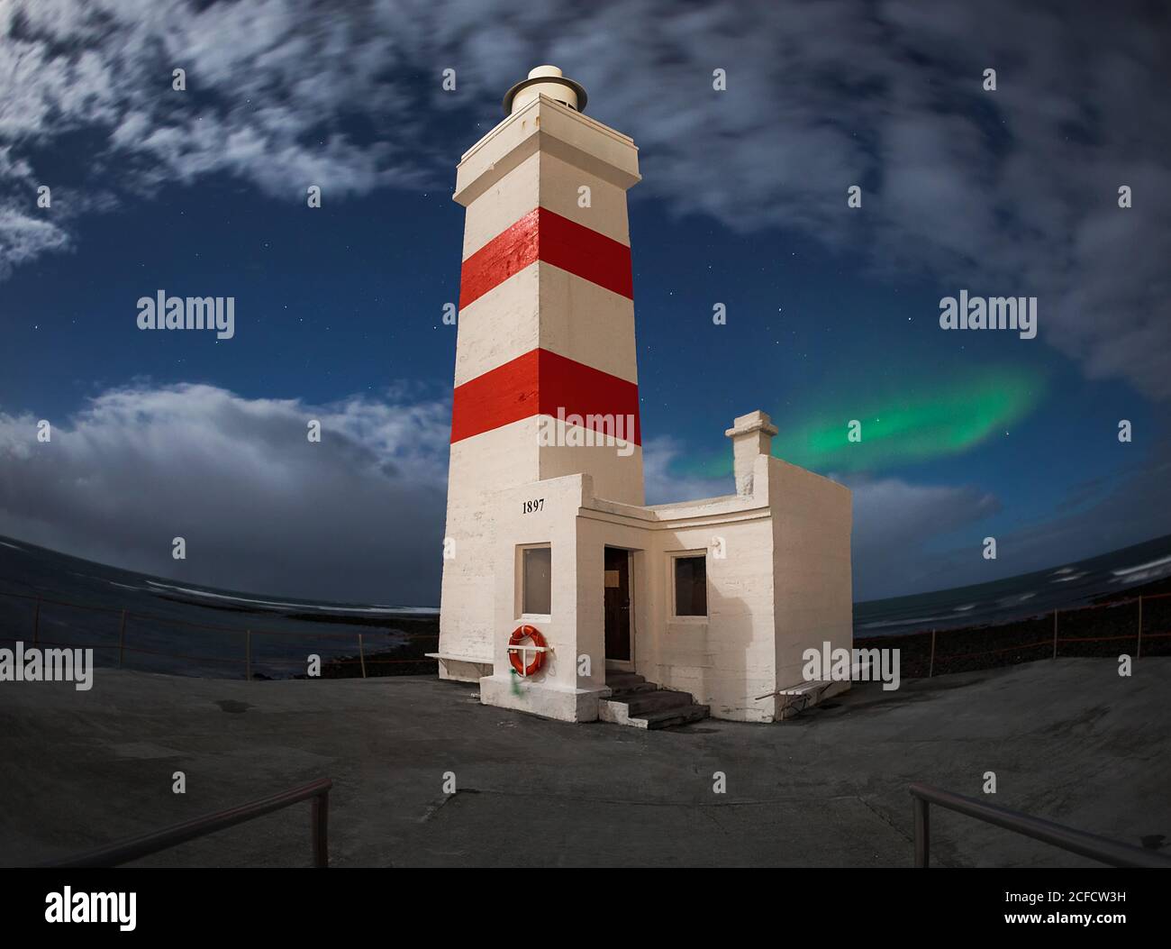 White beacon with striped tower located on seashore against blue night ...