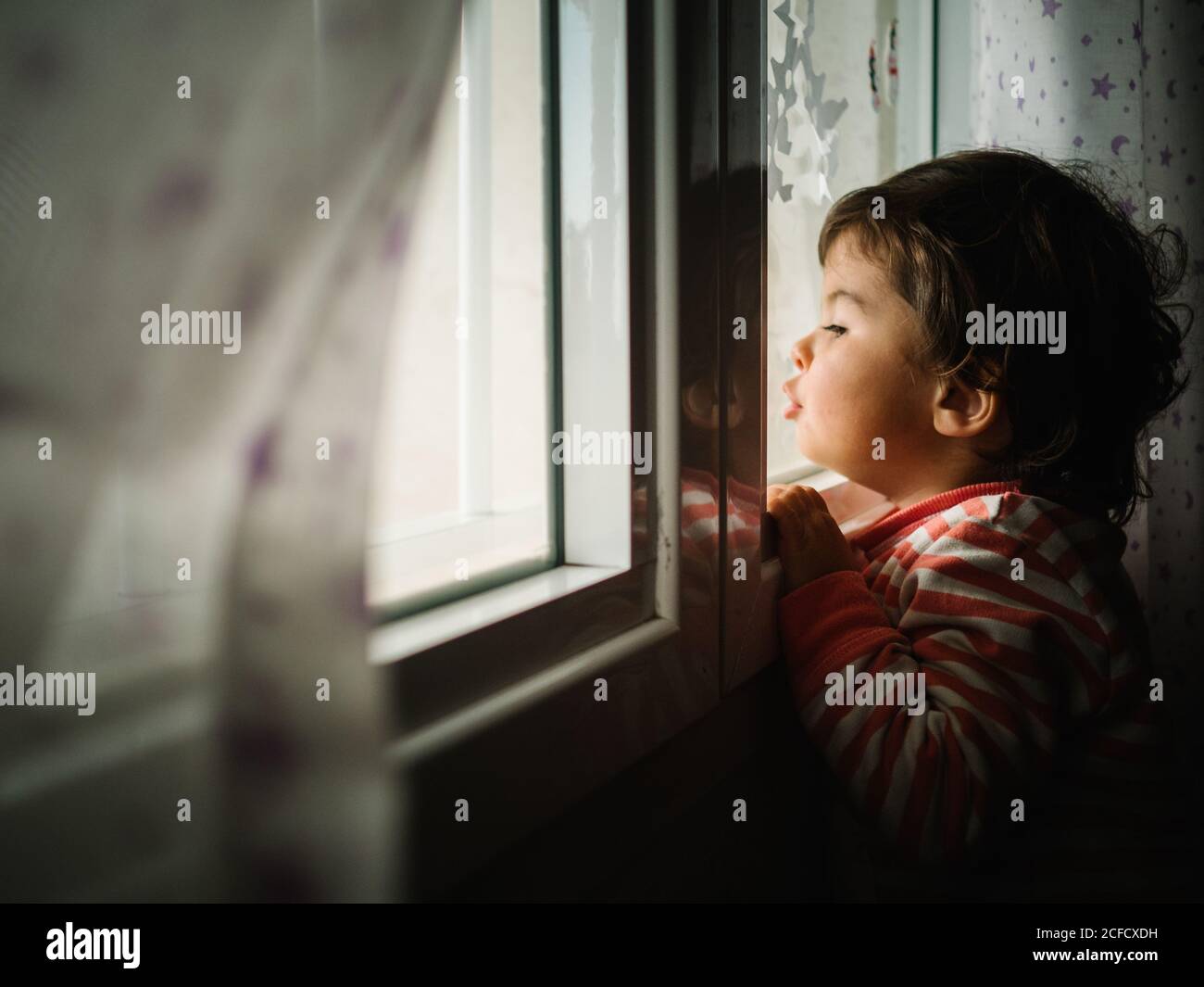 small girl peering through window at home Stock Photo - Alamy