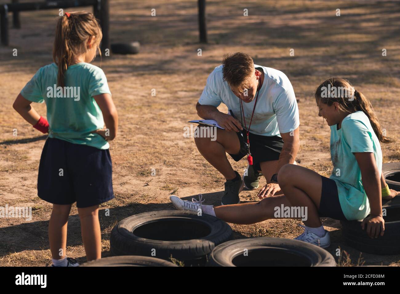 Male fitness coach looking at injured leg of a girl at a boot camp ...