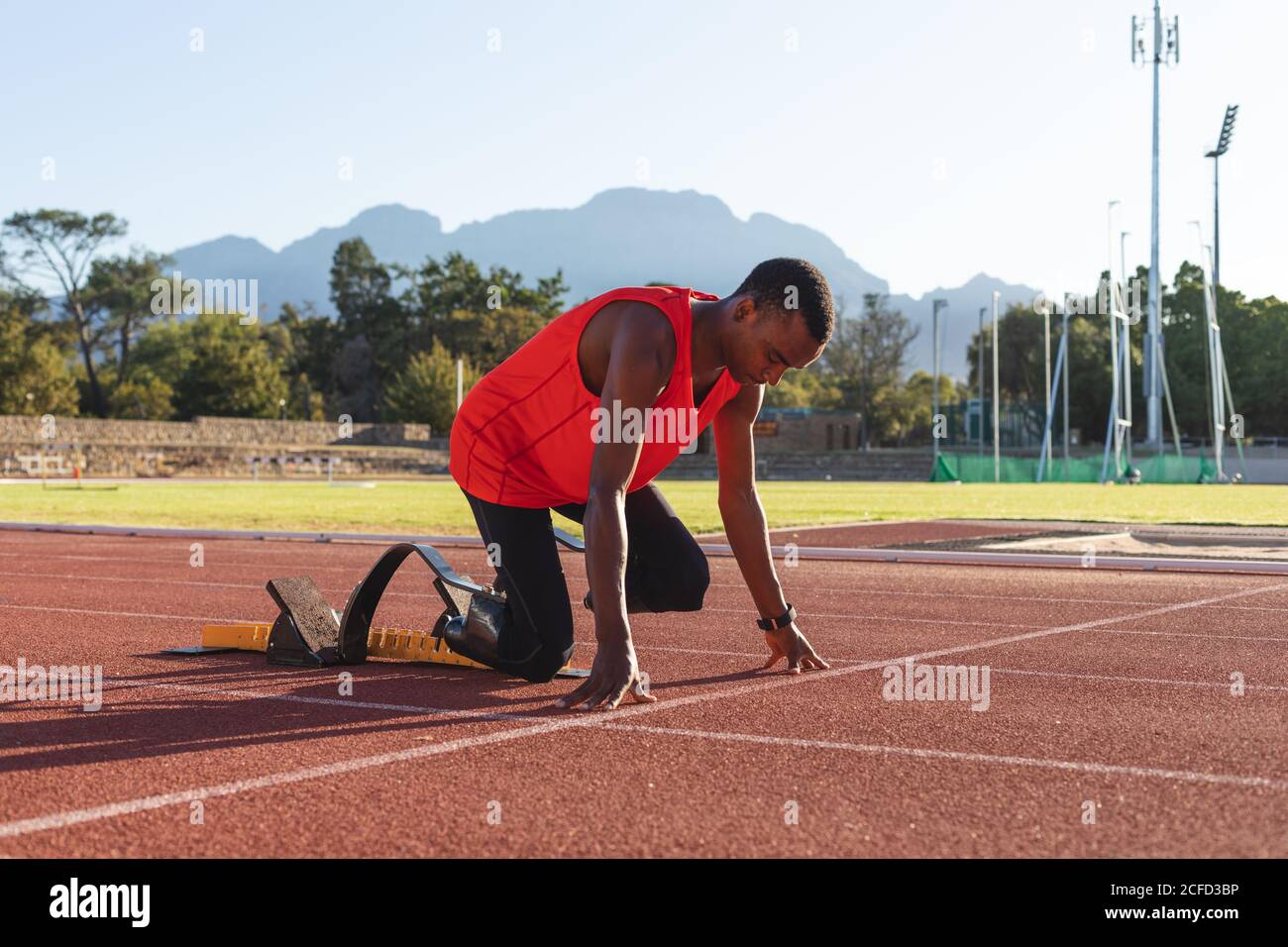 Male athlete with prosthetic leg bending on starting blocks before the ...