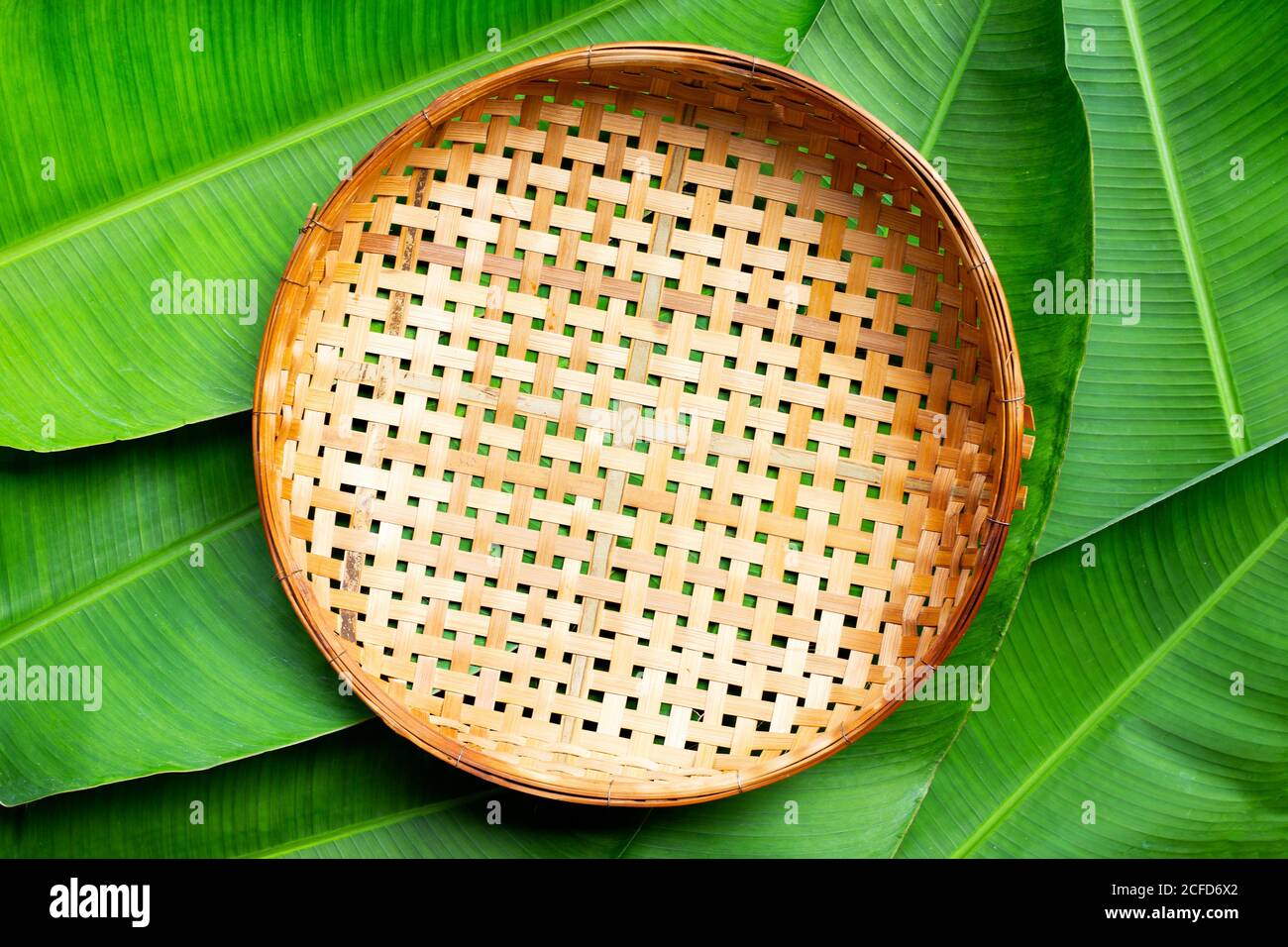 Empty wooden bamboo threshing basket on banana leaves background. Top ...