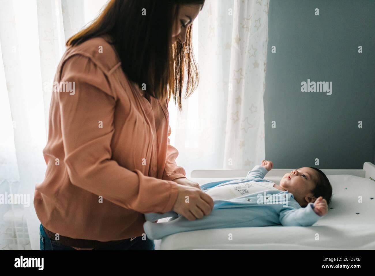 Side view young mother dressing newborn baby on changing table at home ...