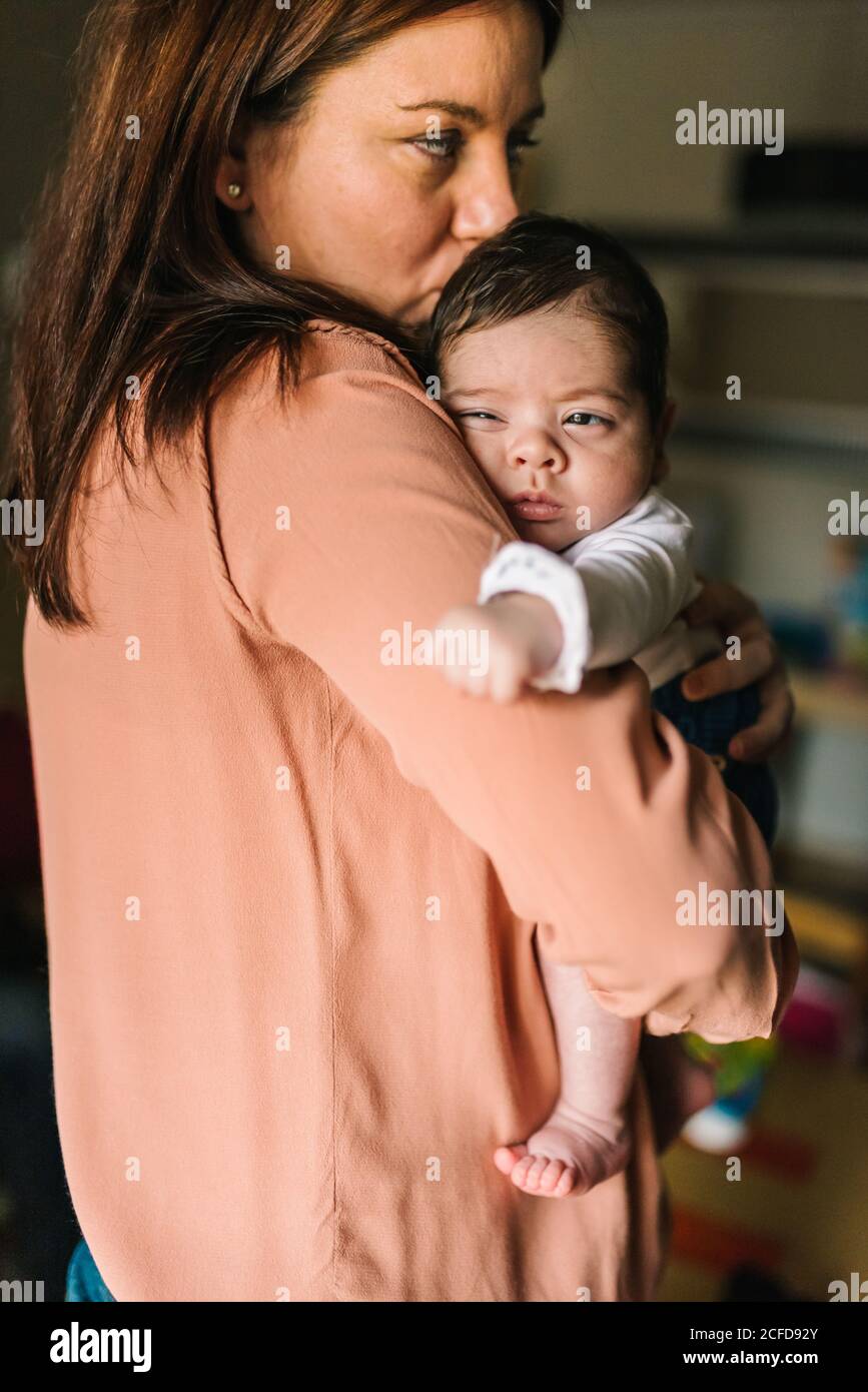 Back view brunette mom hugging cute little baby looking away at home ...