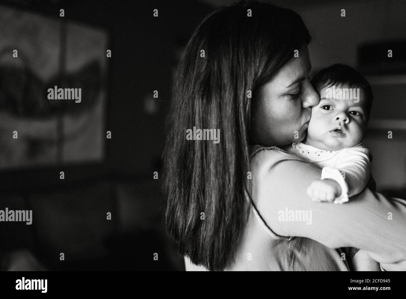 Back view brunette mom hugging cute little baby looking away at home ...