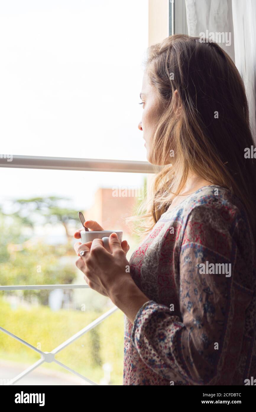 Thoughtful blonde girl in shirt with a cup of coffee looking out the ...