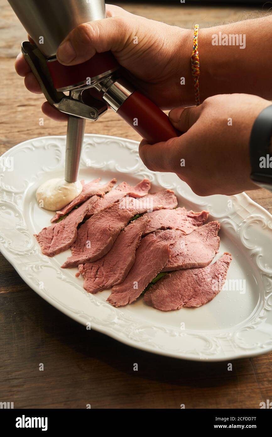 From above of faceless chef adding fluffy sauce on plate with slices of ...