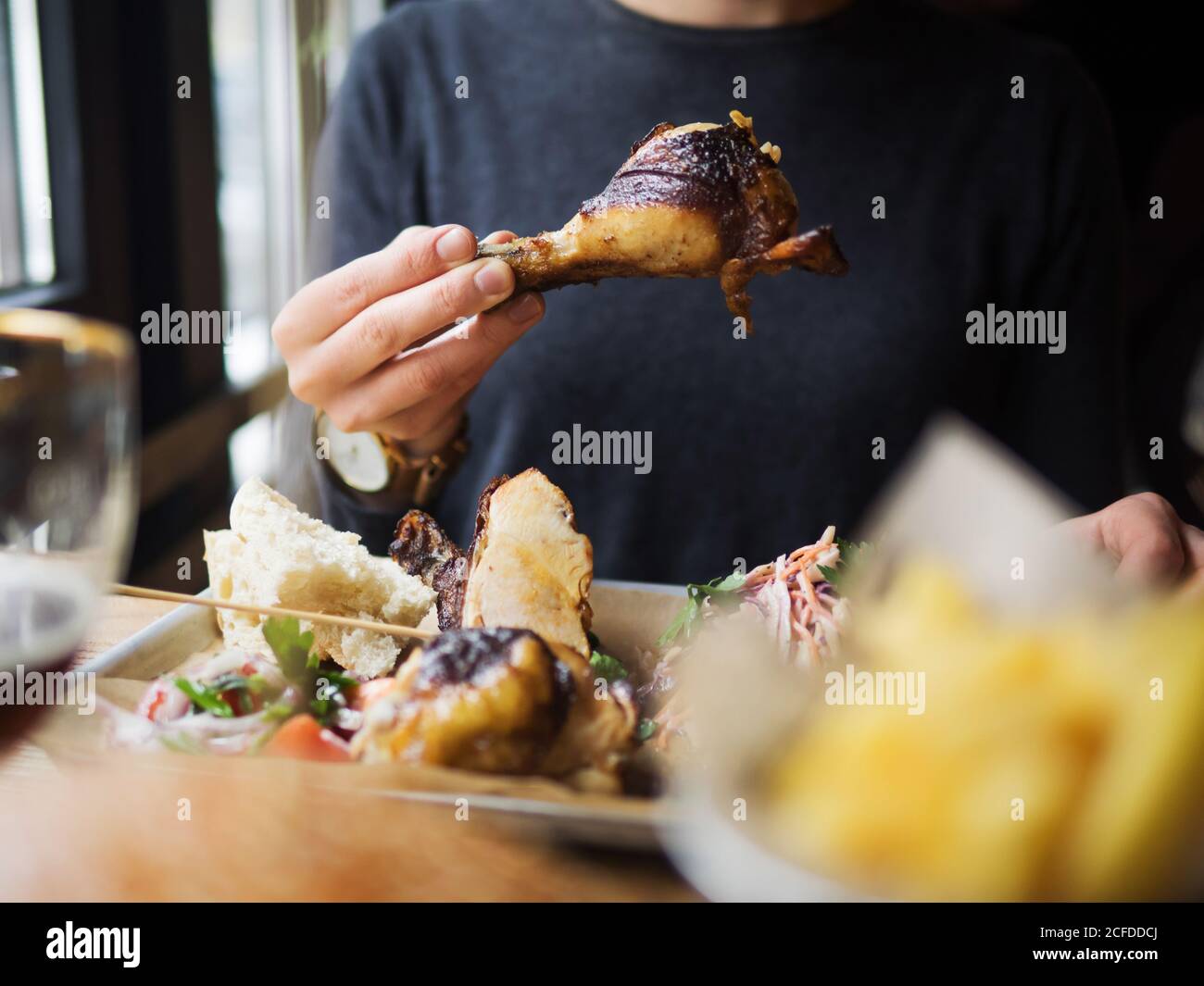 Crop unrecognizable man in casual wear eating grilled chicken leg while ...