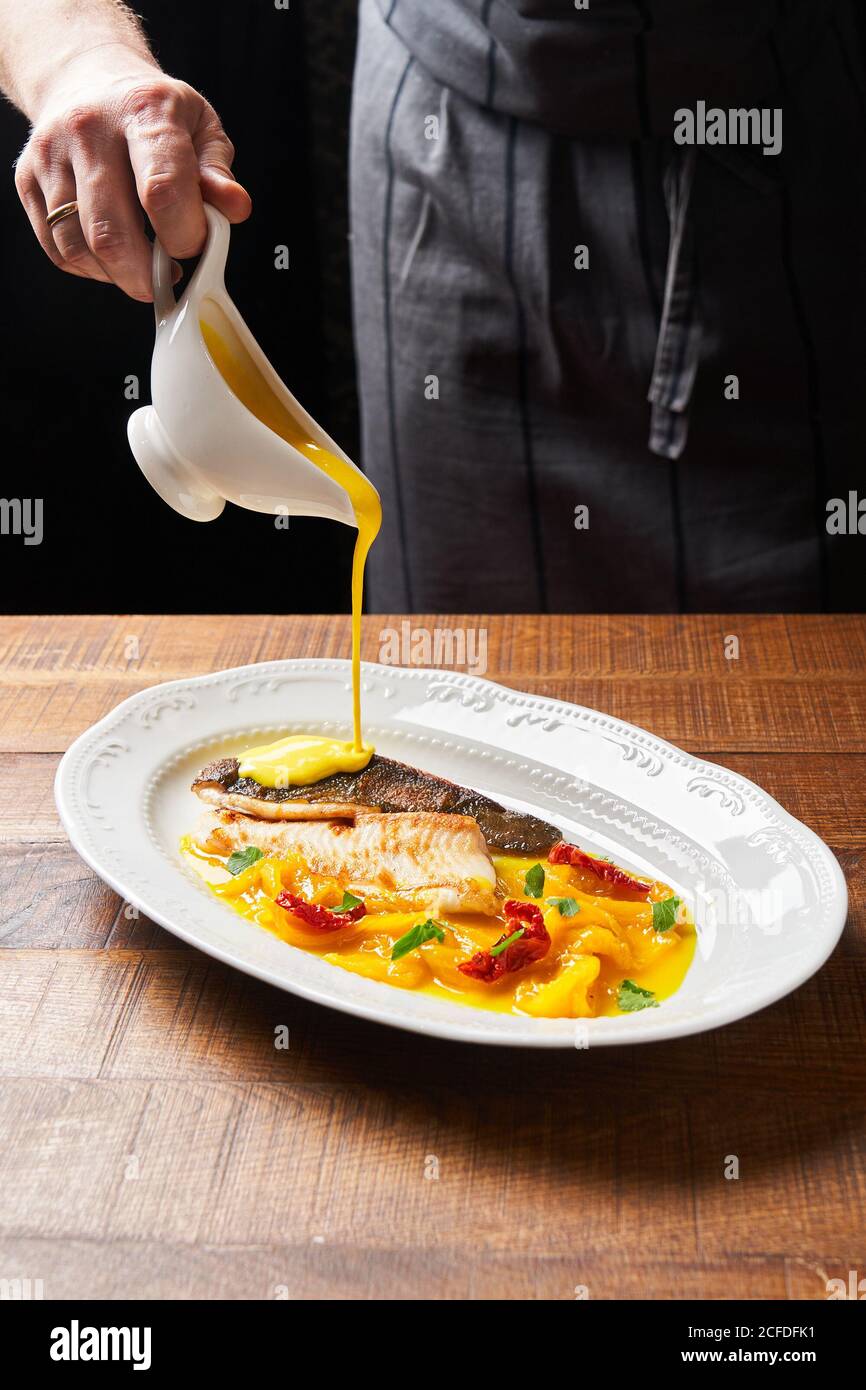 faceless male chef in apron using small ceramic cruet while pouring ...