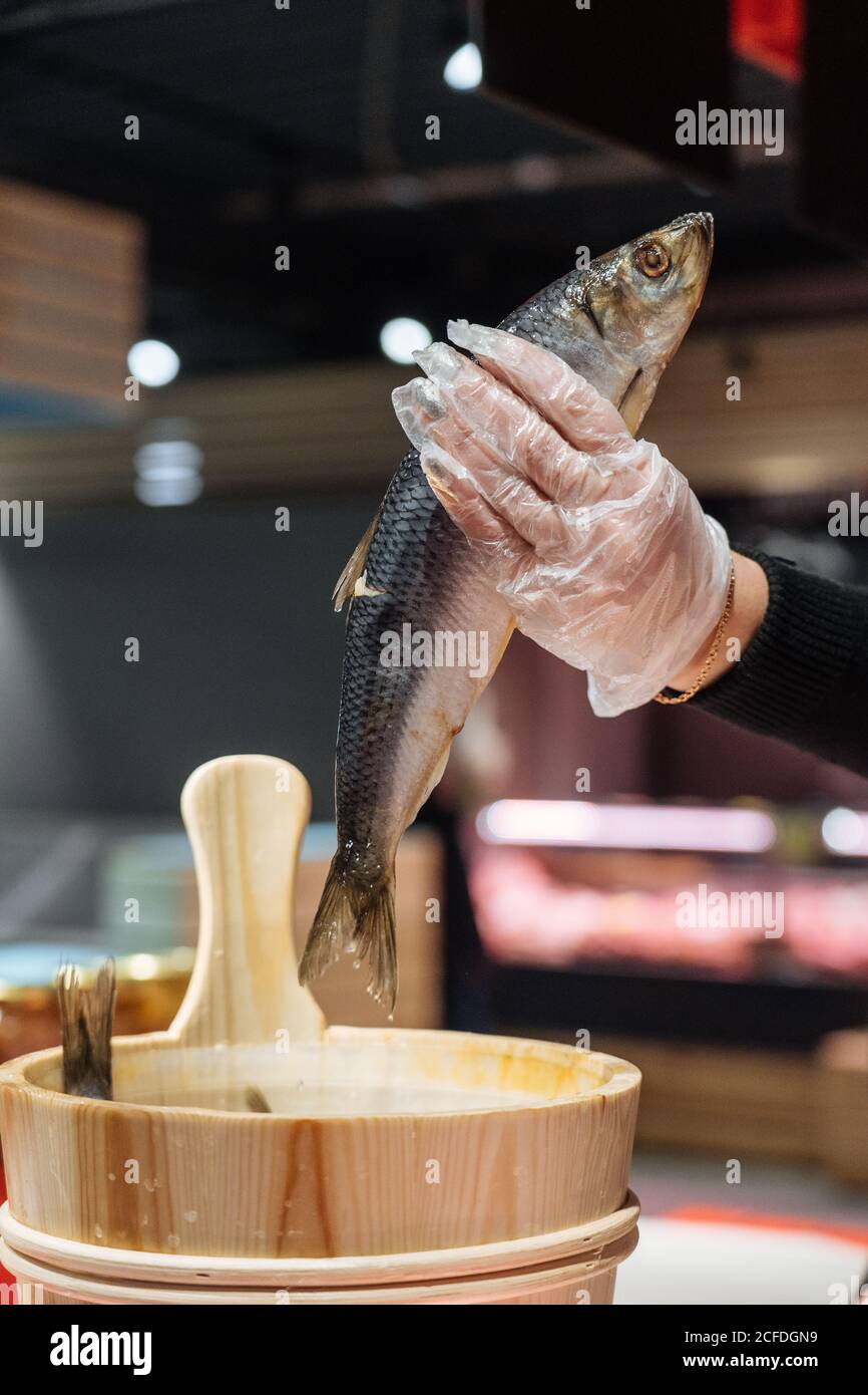 unrecognizable vendor in glove taking fresh fish from wooden bucket ...