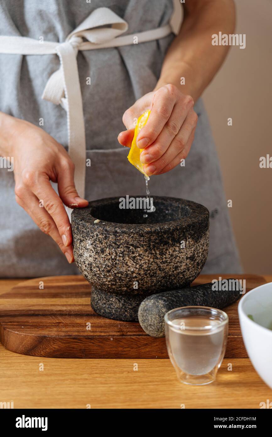 anonymous person in apron squeezing juice of fresh lemon into mortar ...