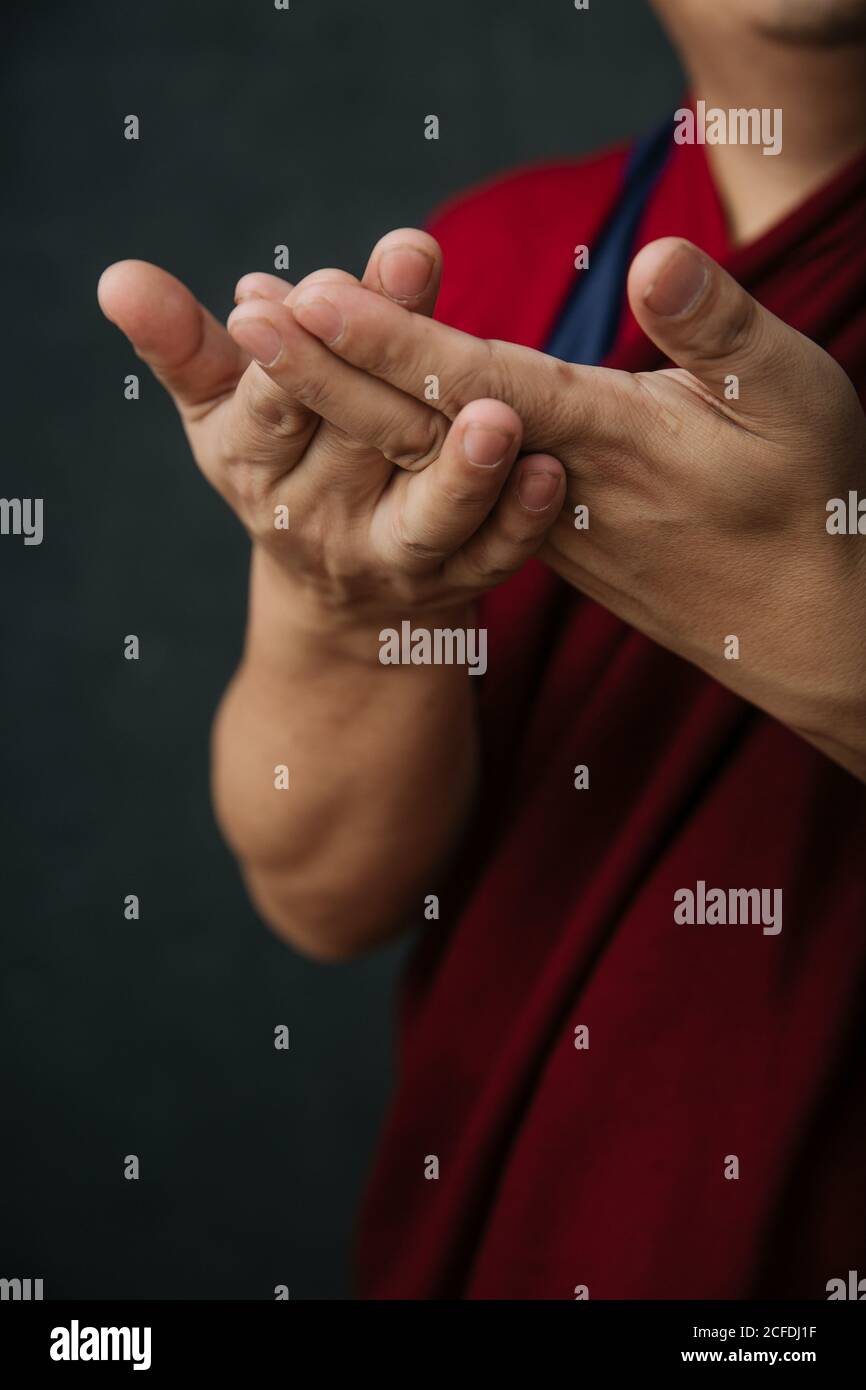 Closeup of hands of crop praying Tibetan monk in traditional red robe ...
