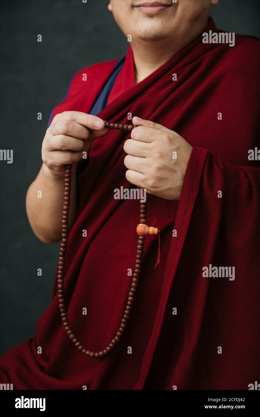 Side view of crop Buddhist monk in traditional red clothes holding ...