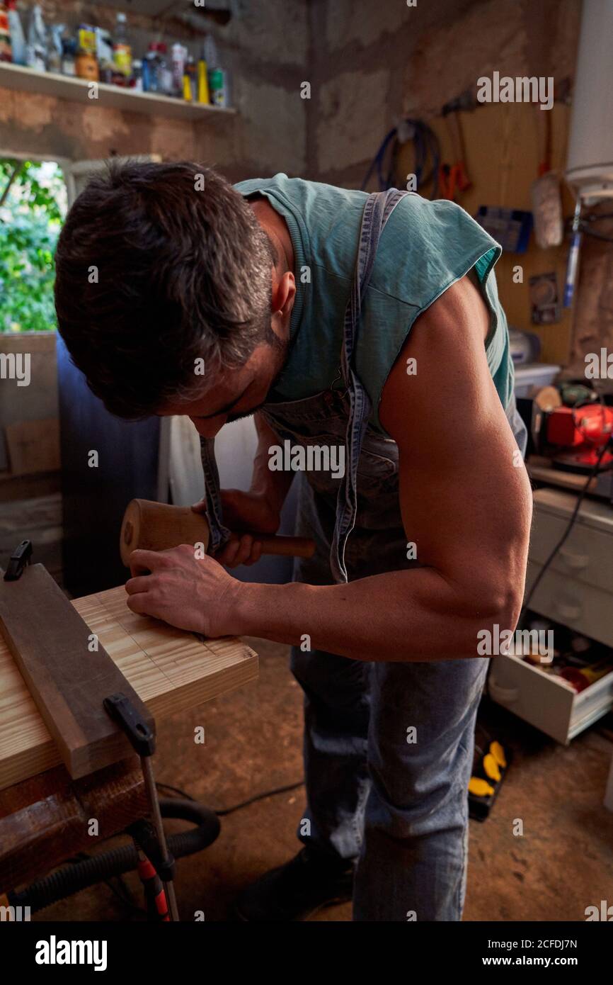 Side view of workman using wooden mallet while working with wooden ...