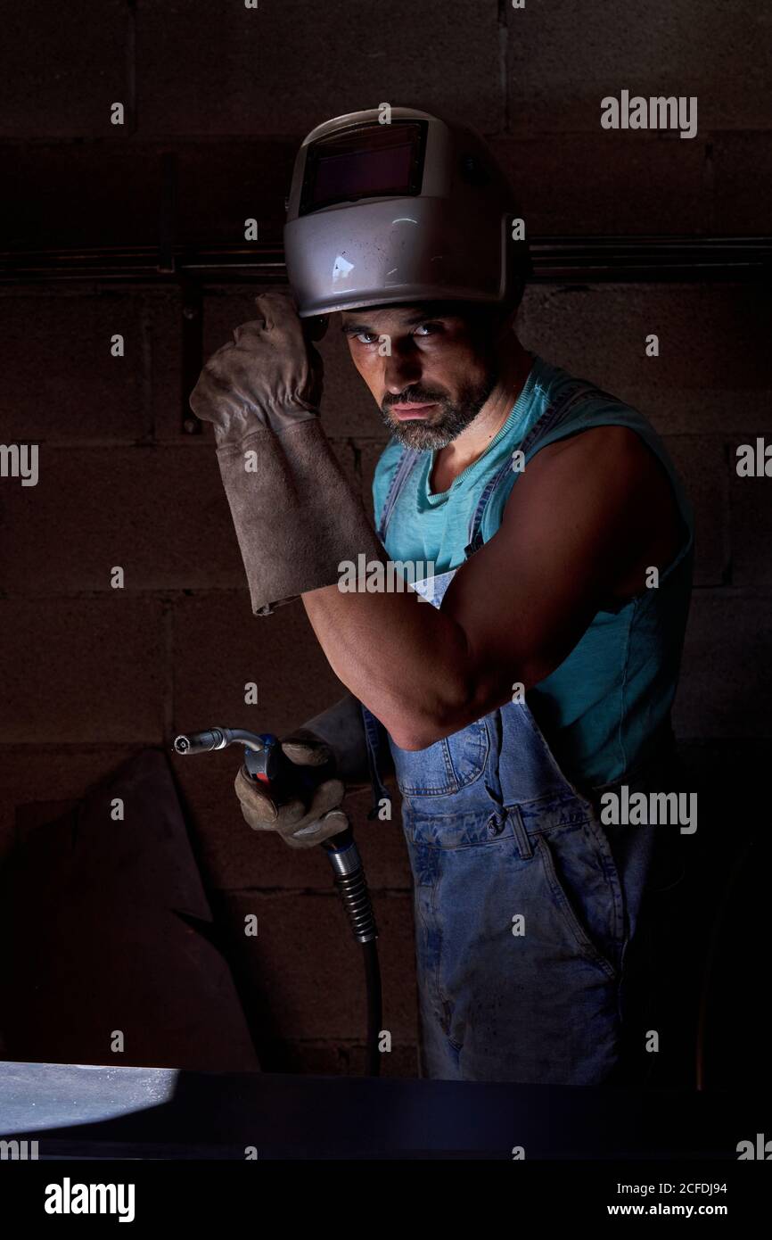 Professional man with welding mask on head wearing jeans overalls and ...