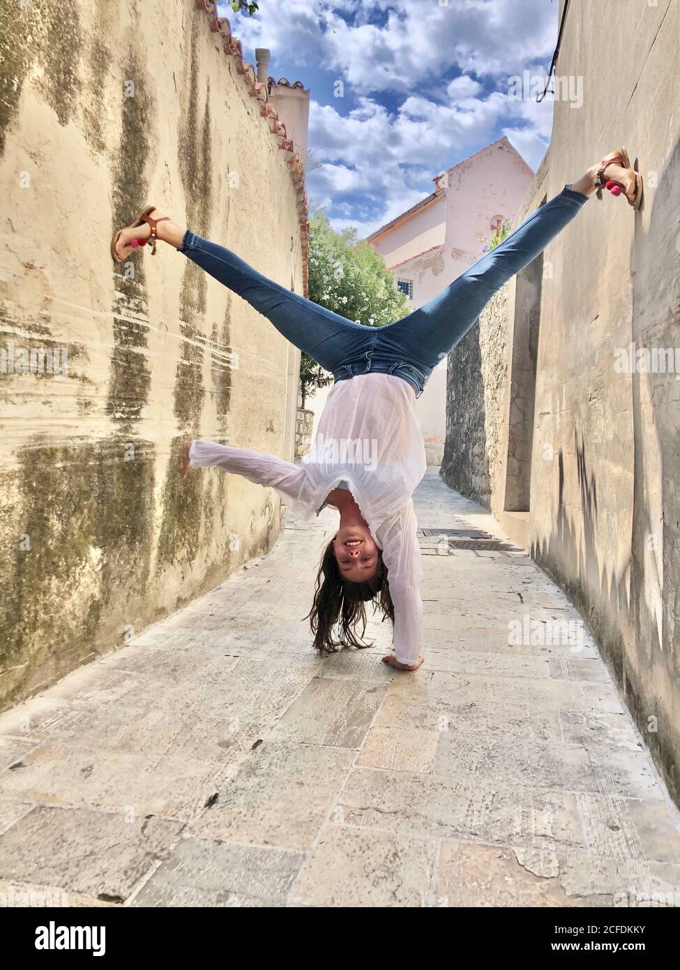 One-handed handstand, young woman, old town, alleys, blue sky, stone ...