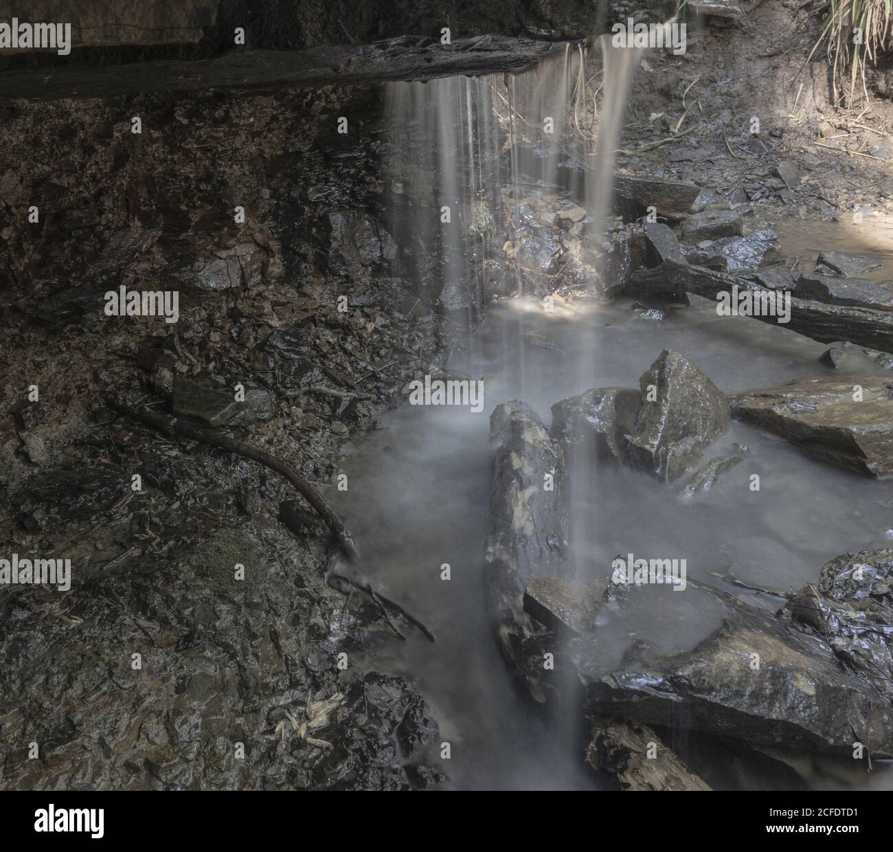 A flowing waterfall from behind a rock ledge into a pool of water Stock ...