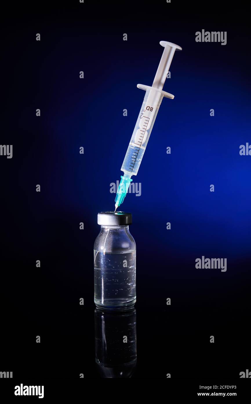 Syringe with needle inserted in cap of bottle with vaccine in dark room ...