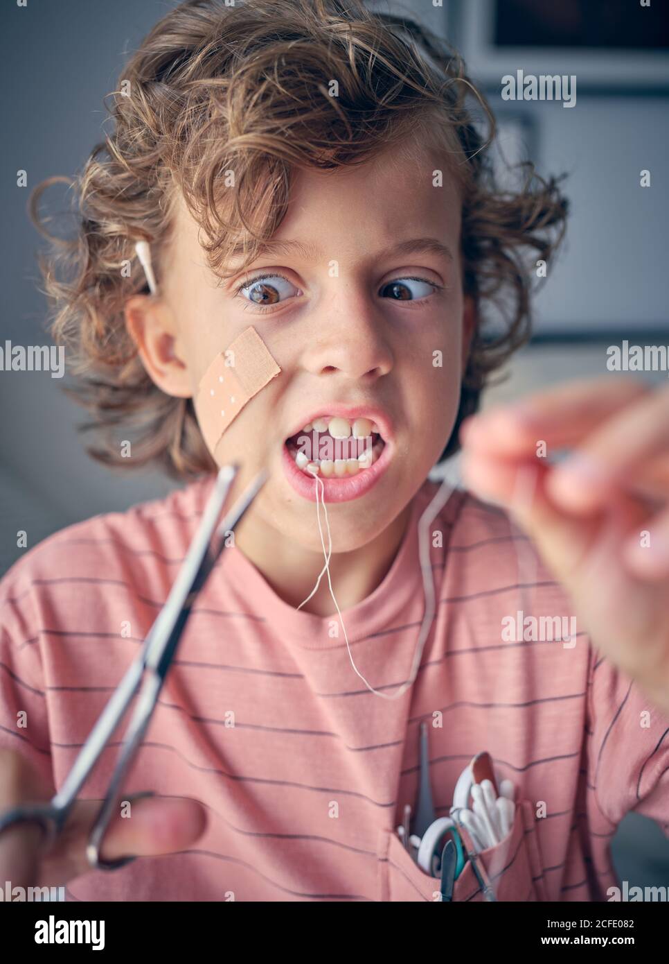 Excited curly kid pulling dental floss for which milk tooth tied with ...