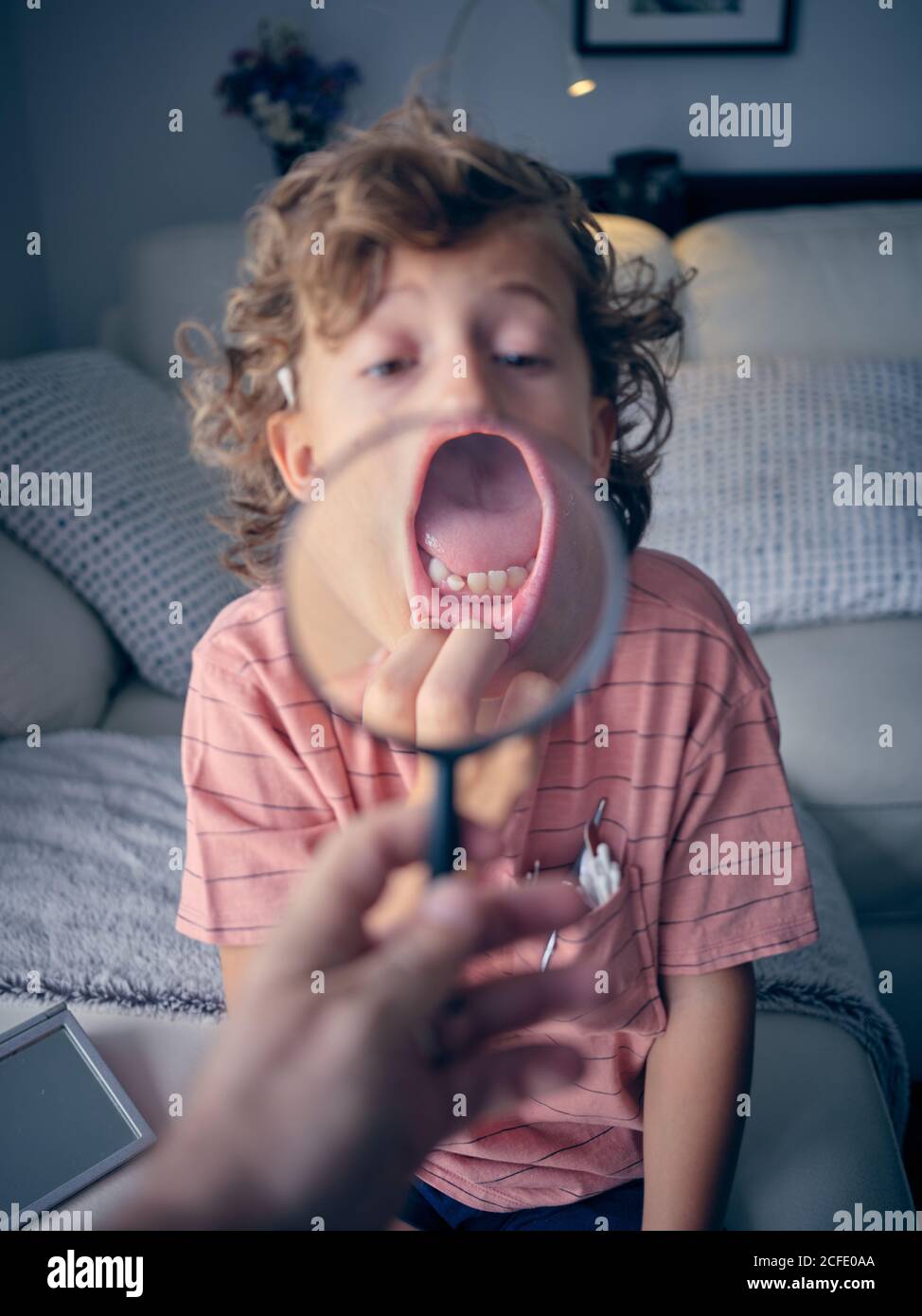 Surprised curly child showing tooth with mouth wide open pulling lower ...