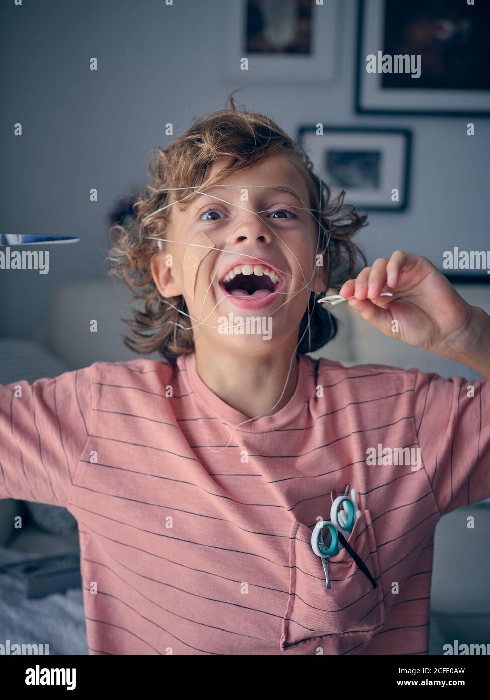 Excited curly kid pulling dental floss for which milk tooth tied with ...