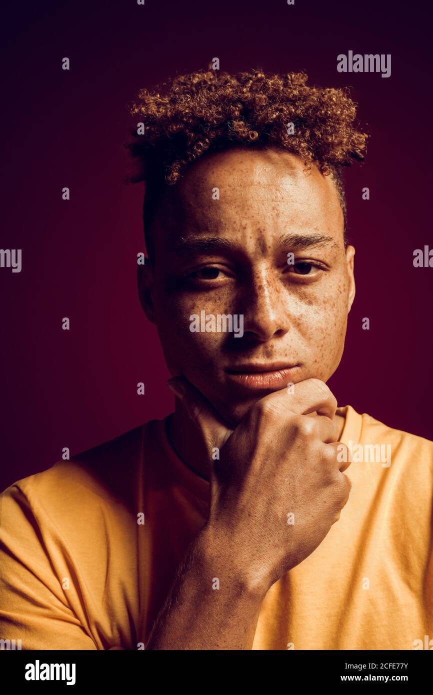 Freestyle. Mulatto freckled guy standing isolated on dark red in yellow ...