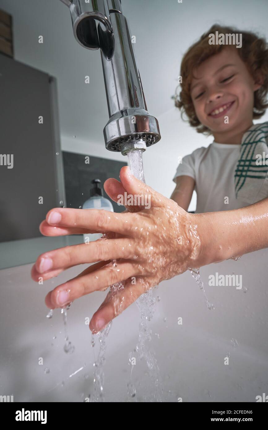 From below boy with towel on shoulder washing hands under running water ...