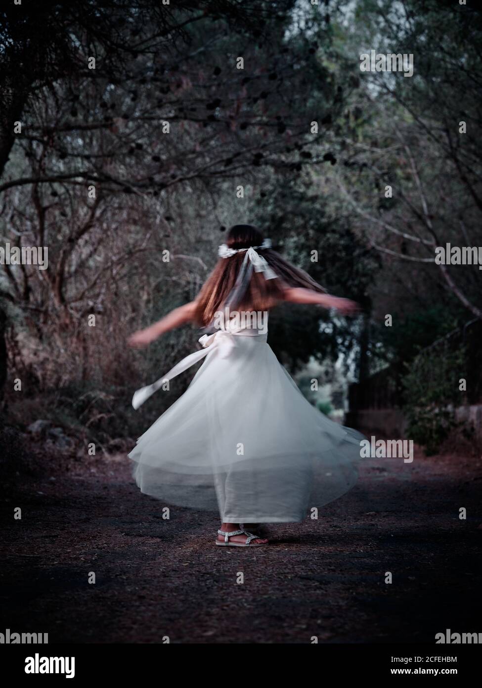 Back view of little lonely girl in long white dress dancing on road in ...