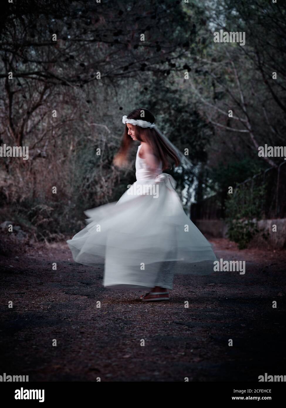 Side view of little lonely girl in long white dress dancing on road in ...