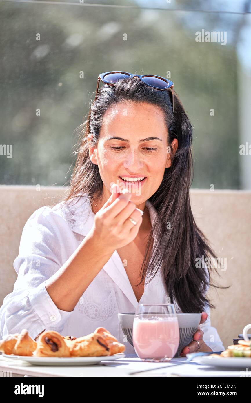 Pretty friendly lady sitting at served table on open sunlit terrace and ...