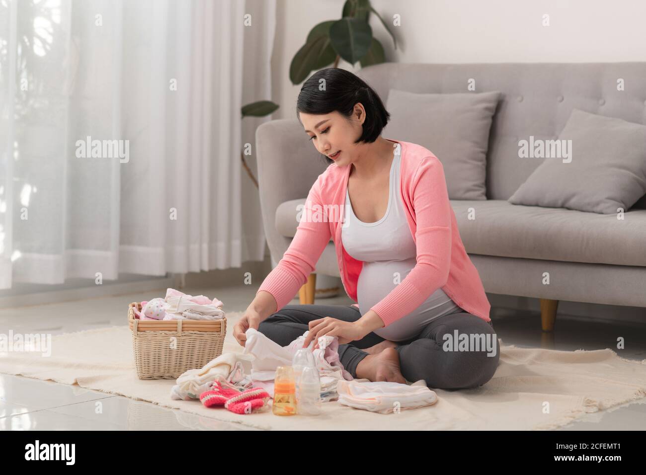 Cheerful pregnant preparing baby clothes and making to do list, getting ...