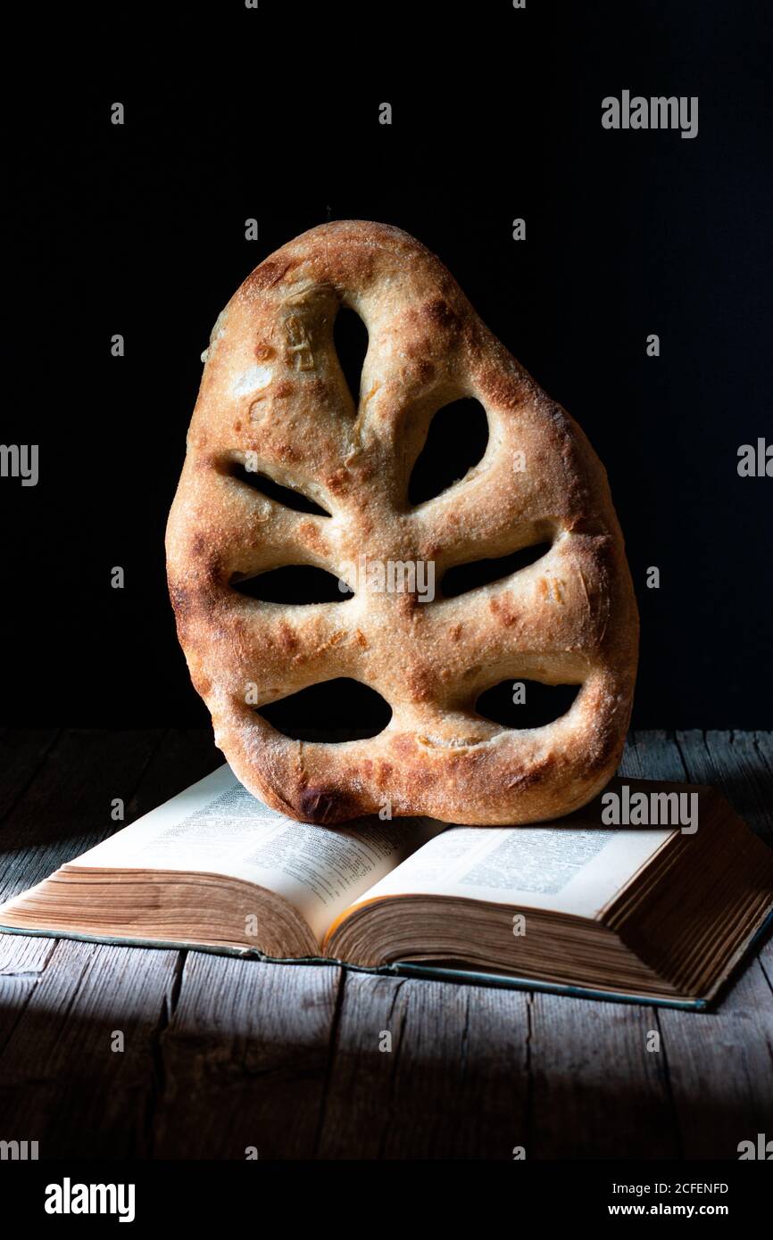 Loaf of fresh fougasse bread placed on open recipe book on wooden table ...