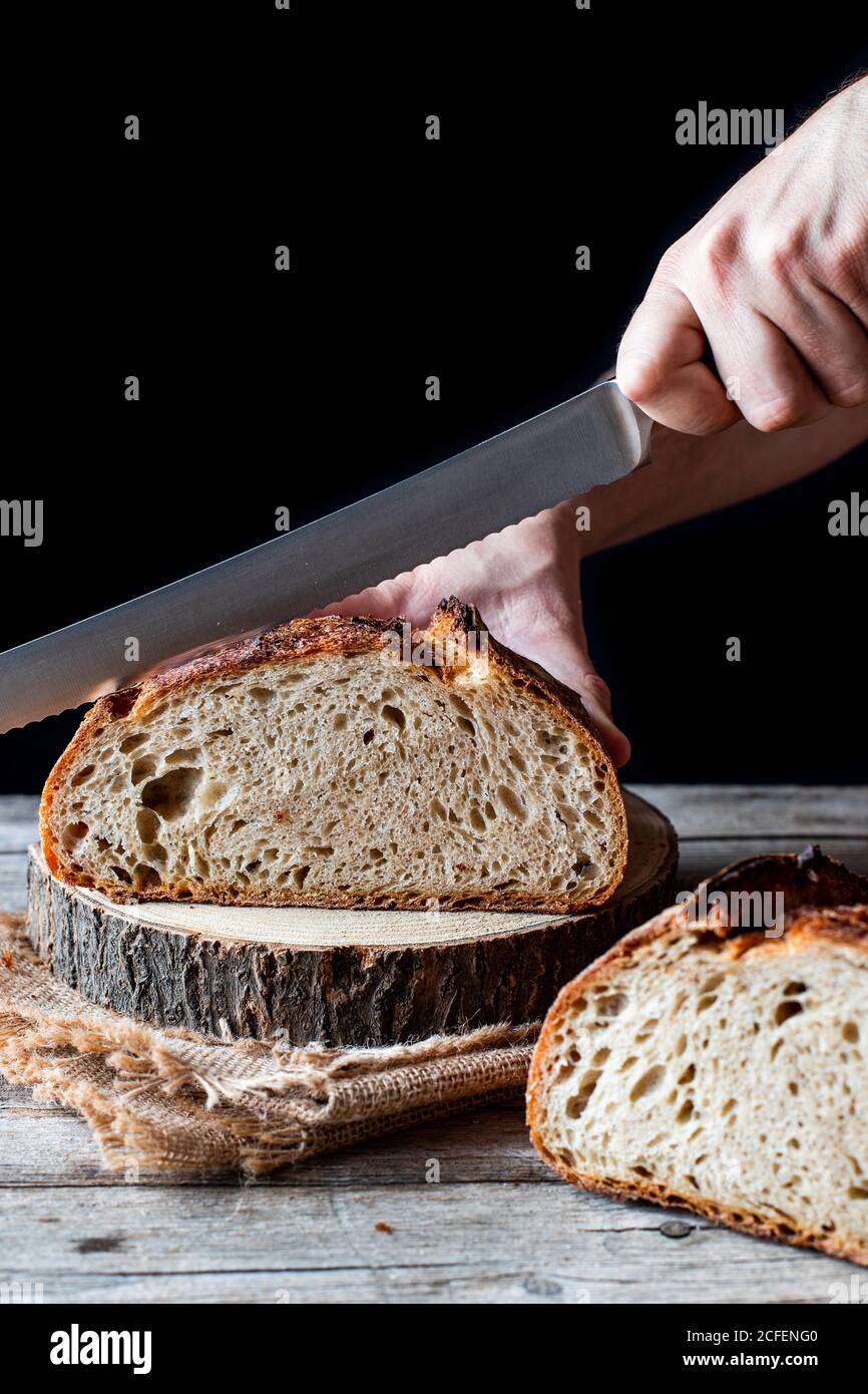 unrecognizable person using knife to cut loaf of fresh sourdough bread ...