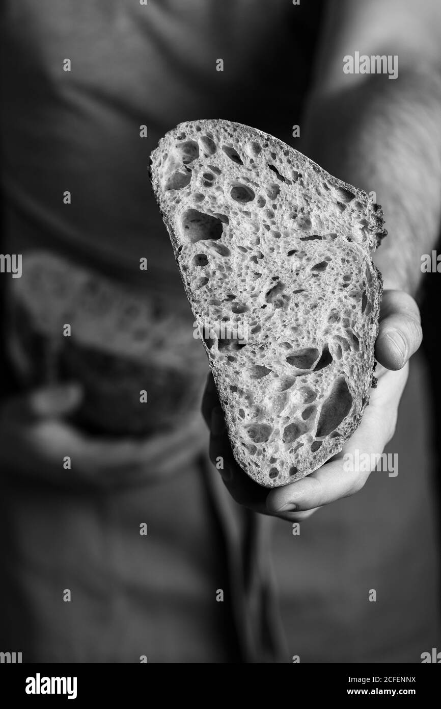 Crop male baker in apron holding cut in half loaf of fresh healthy ...