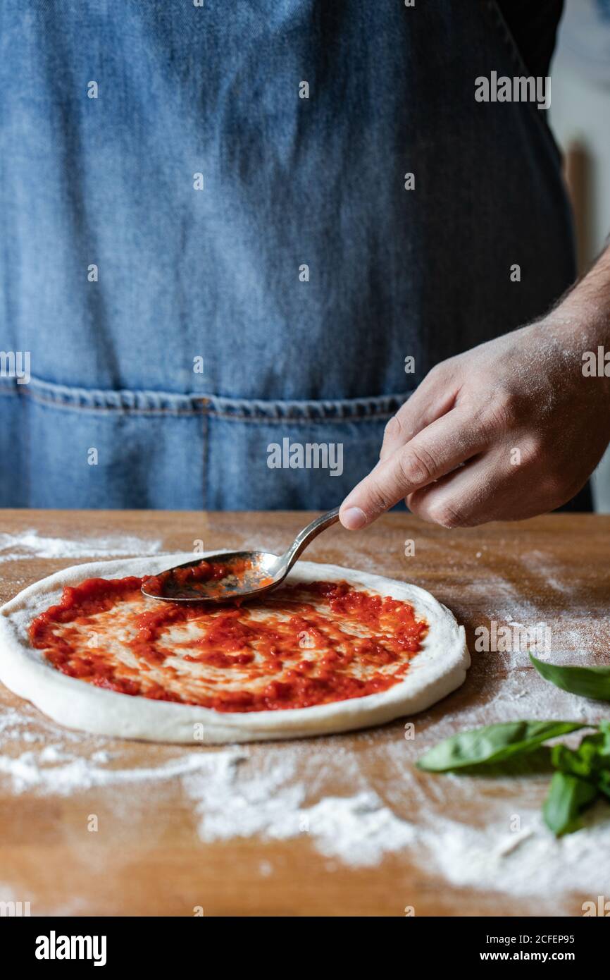 anonymous chef smearing fresh tomato sauce on raw dough while cooking ...