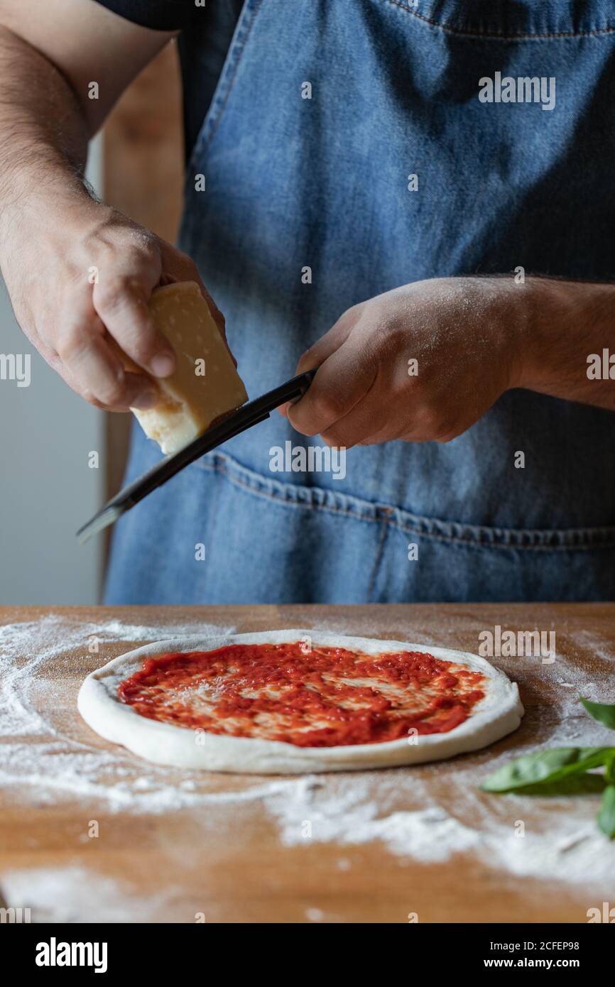 unrecognizable guy in apron grinding fresh cheese on dough with tomato ...