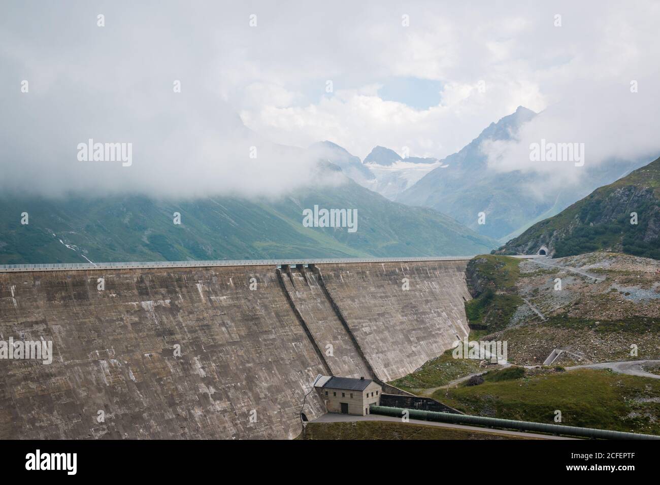 High alpine road on big dam on background with misty cloudy mountains ...