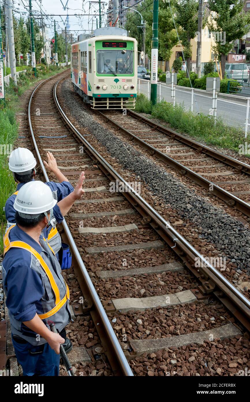 Workmen wave at a tram or street car on the Toden Arakawa Line, known ...