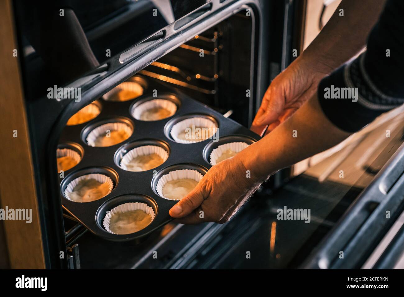 High angle of crop housewife putting muffin tray with dough in paper ...