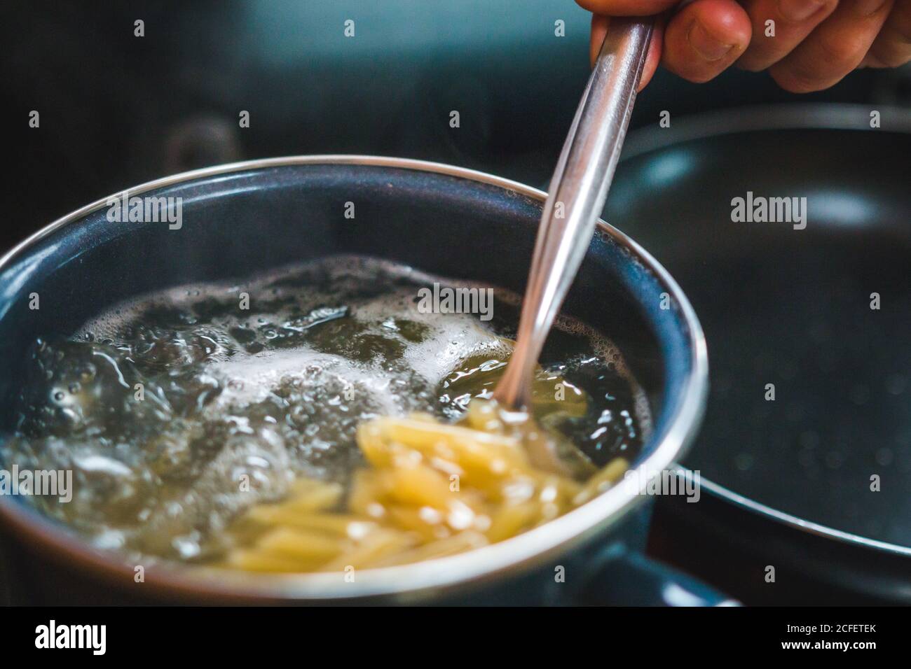 Closeup of crop unrecognizable hand cooking raw pasta spilling from box ...