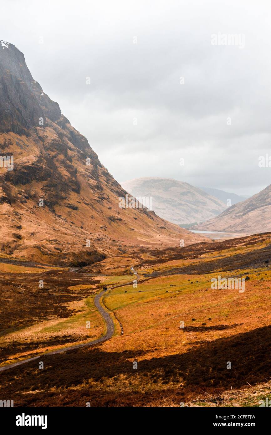 Narrow curvy road running through hilly terrain with dry grass among ...