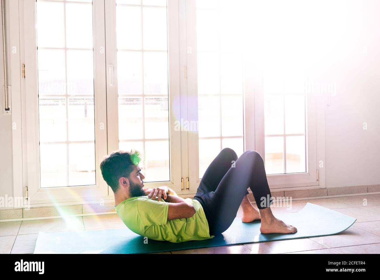 High angle side view of determined male athlete in sportswear doing abs ...