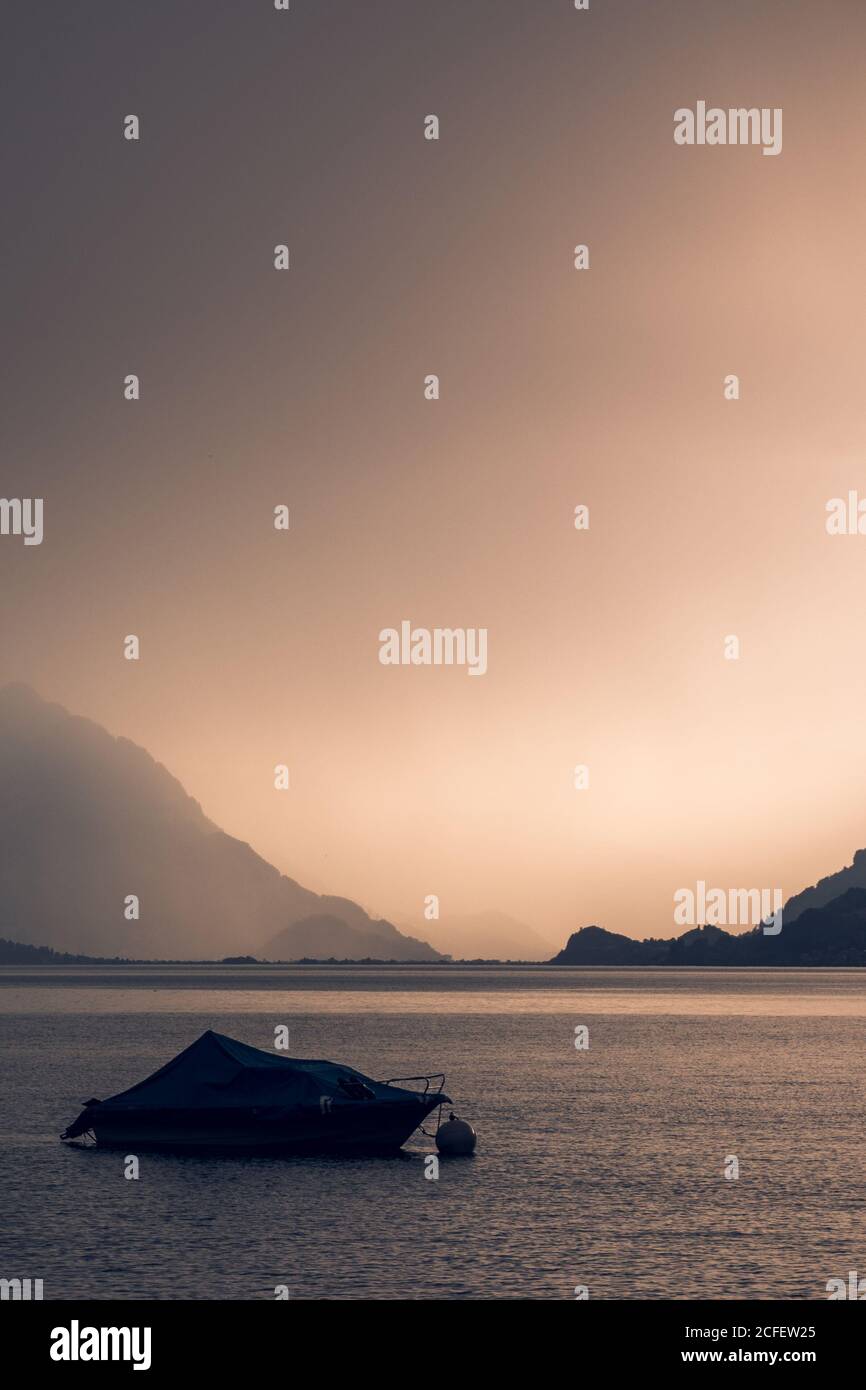 Calm landscape of dark boat in wavy water under gray cloudy sky in ...