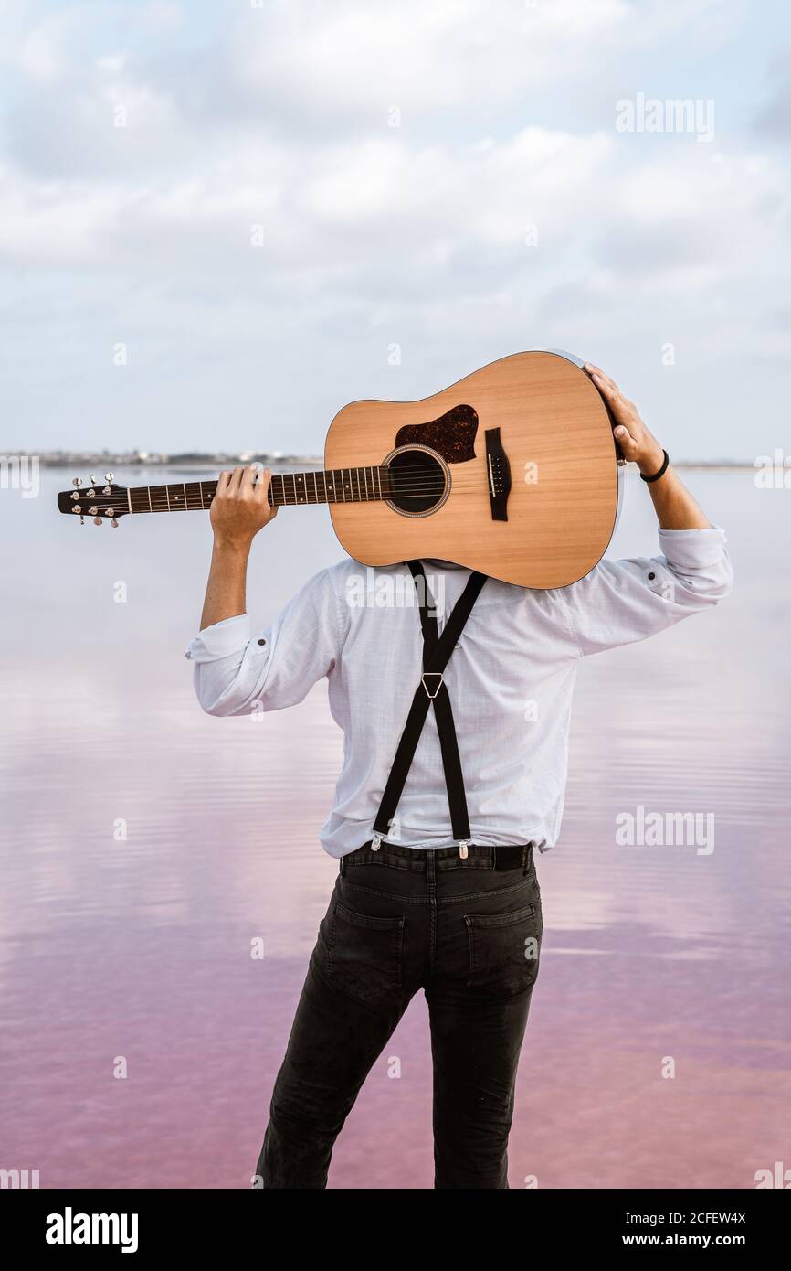 From behind man in white shirt holding acoustic guitar behind back ...