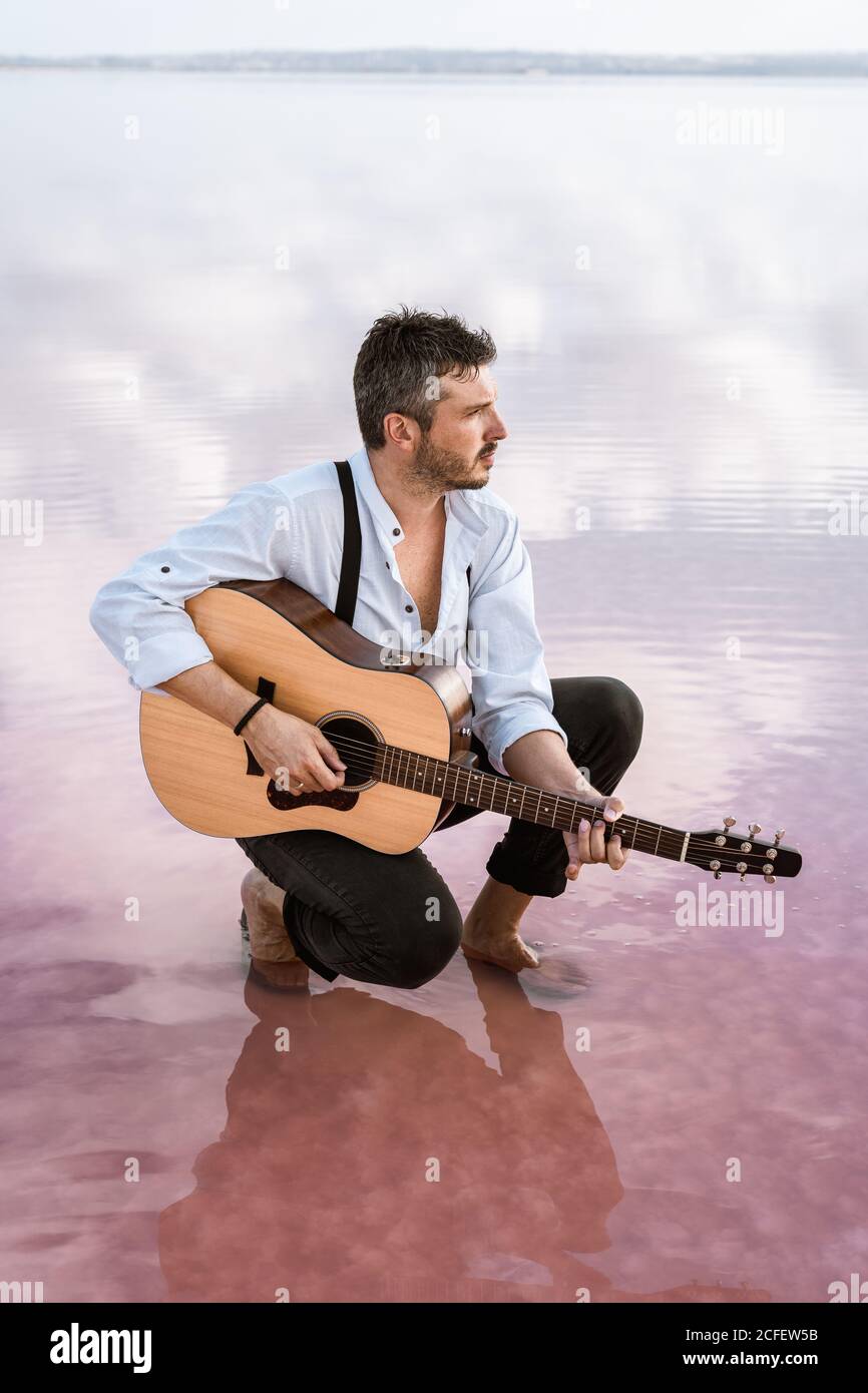 Wistful man in white shirt and suspenders carrying acoustic guitar and ...