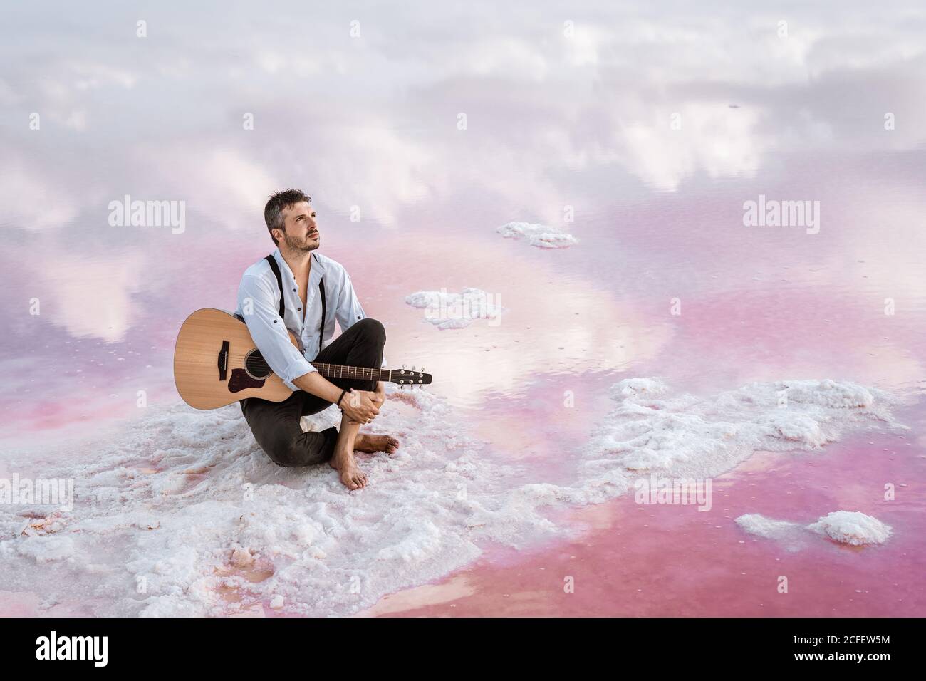 Wistful man in white shirt and suspenders carrying acoustic guitar and ...