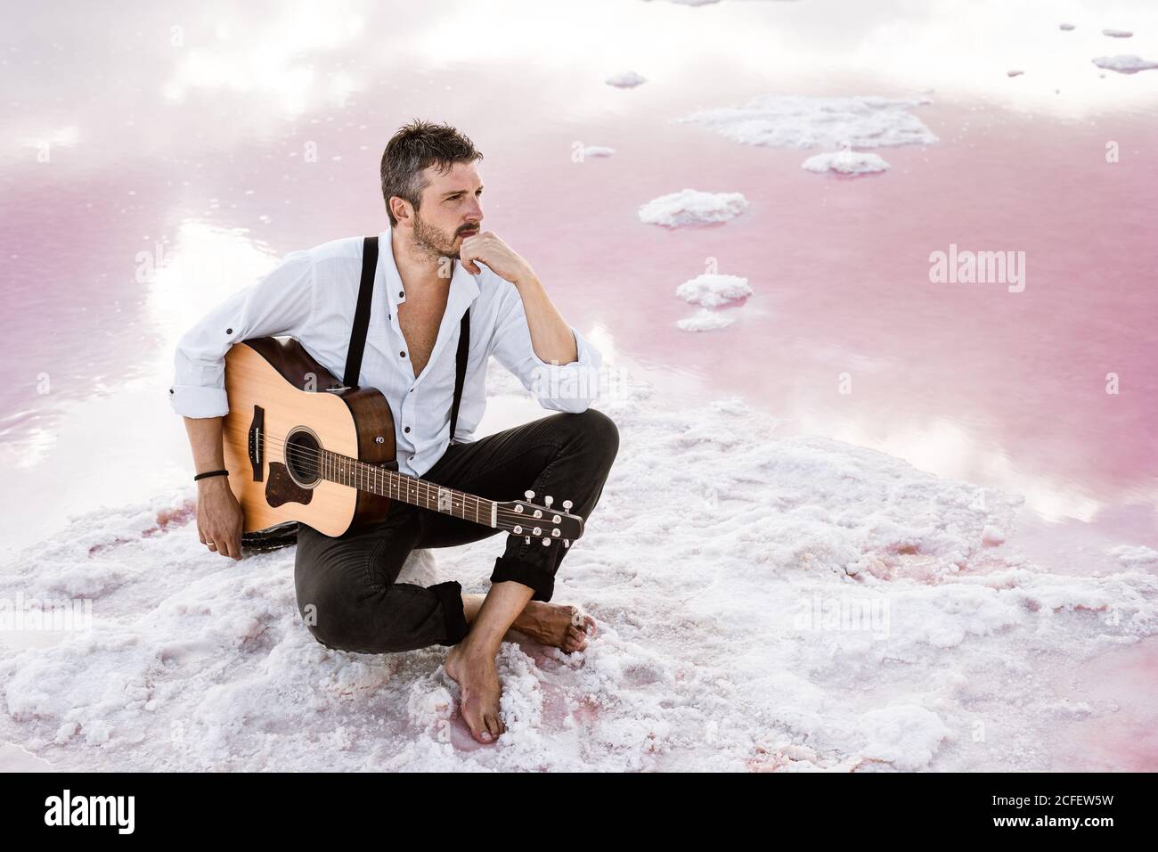 Wistful man in white shirt and suspenders carrying acoustic guitar and ...