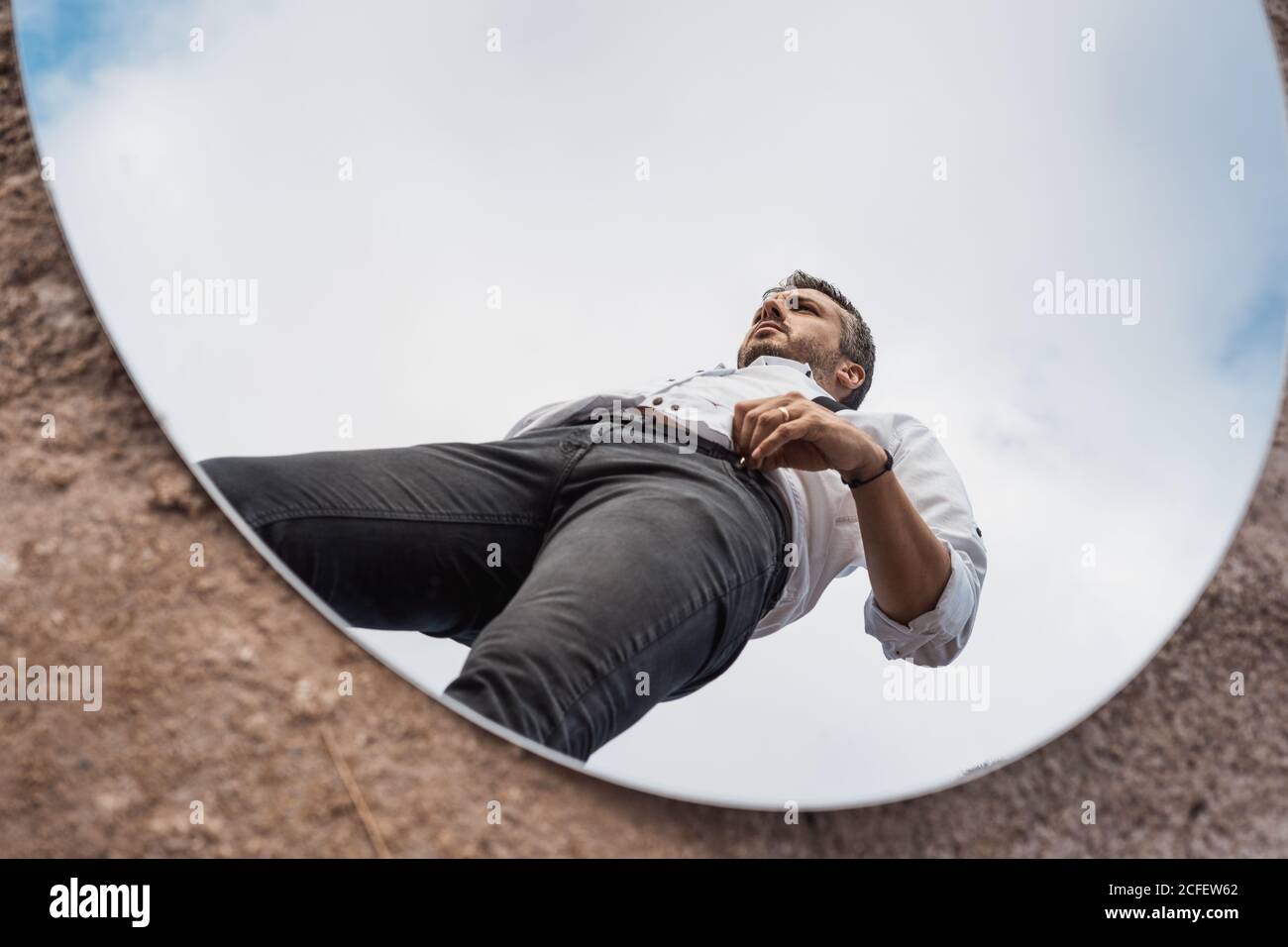 Low angle reflection of dreamy man in shirt and suspenders standing ...